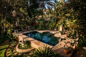 Piscina rodeada por vegetação exuberante, um deck de pedra e uma fonte de pedra.