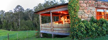 Uma cabana de madeira rústica com varanda coberta, paredes de pedra e um jardim exuberante.