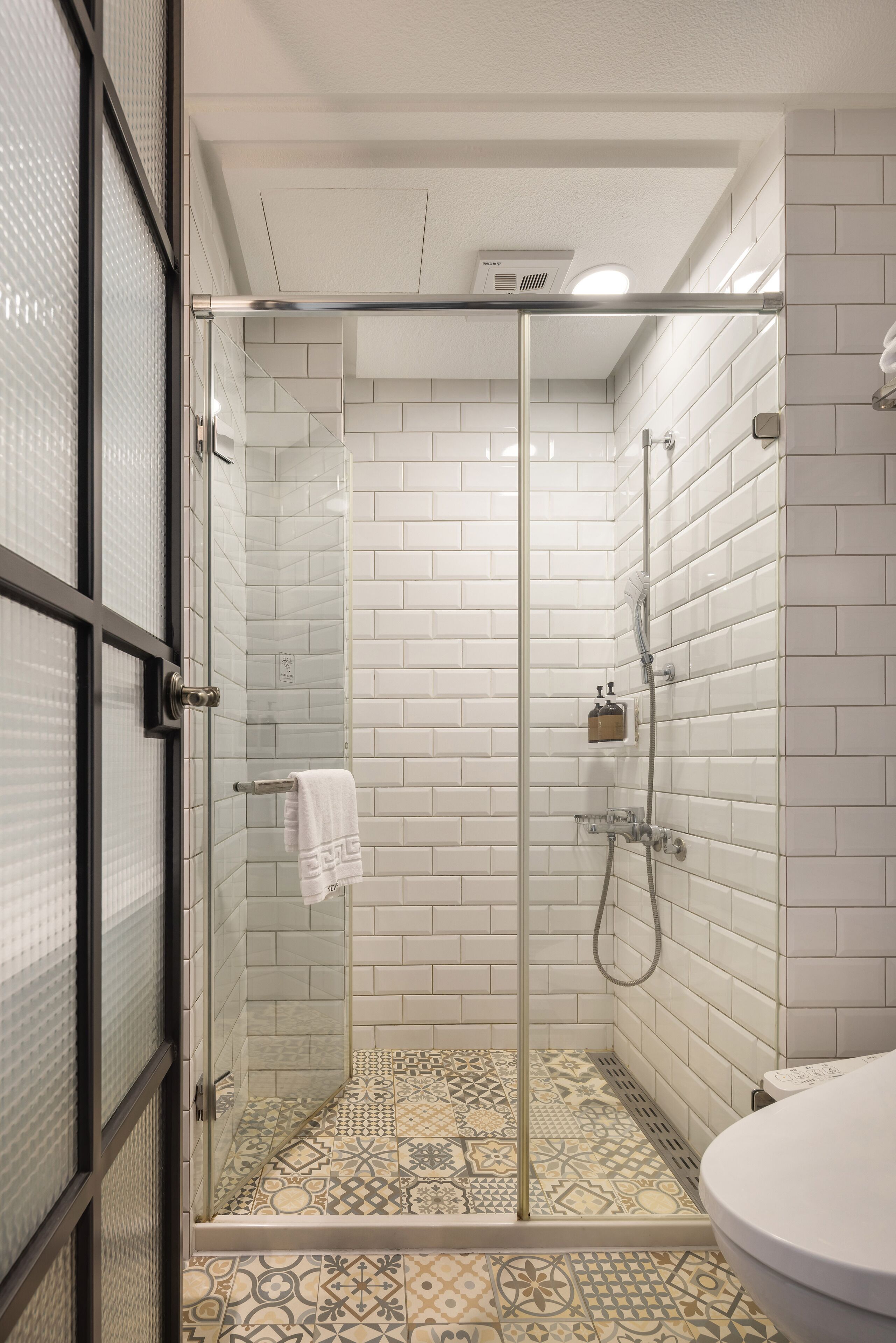 Um chuveiro com paredes de azulejos brancos e chão estampado, todo envolvido em vidro.