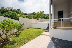 Uma casa moderna com um pequeno jardim, um deck de madeira e uma escadaria que leva a uma varanda.