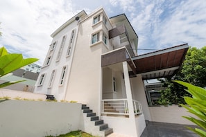 Uma casa moderna de dois andares com telhado plano, varanda coberta e escadaria que leva à entrada.