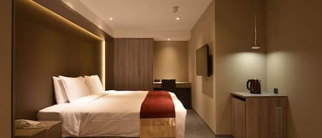 Quarto de hotel com cama, mesa de cabeceira, escrivaninha e um pequeno armário.