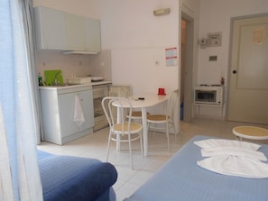 Quarto compacto com cozinha compacta, mesa de jantar com cadeiras, cama e pequena mesa com toalhas.