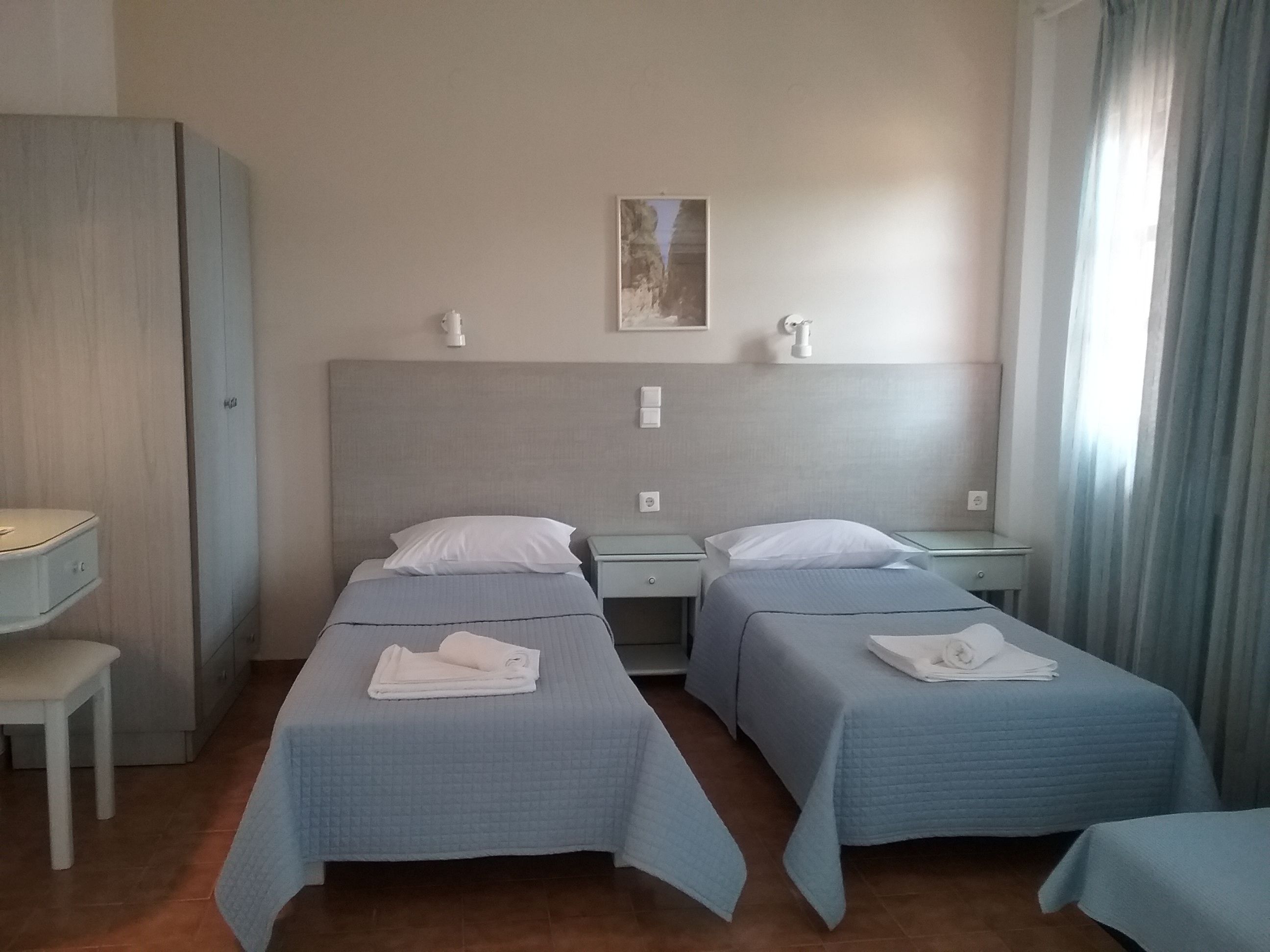 Quarto de hotel com duas camas de solteiro, uma escrivaninha e uma cadeira.