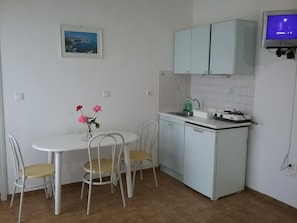 Uma cozinha pequena e branca, com uma pia, uma mesa de jantar branca com quatro cadeiras e um quadro na parede.