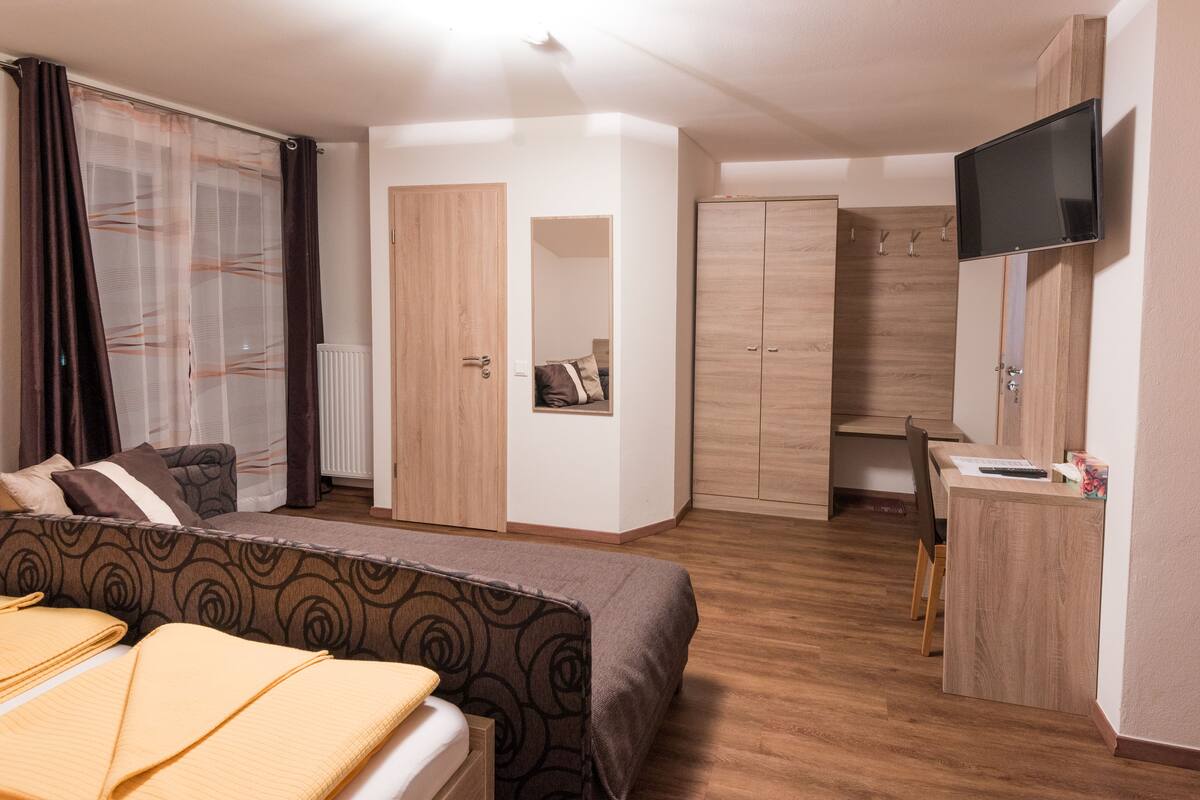 Quarto de hotel com cama, escrivaninha, televisão e guarda-roupa.