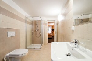 Uma casa de banho moderna com cabine de duche em vidro, lavatório branco e sanita.