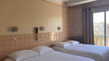 Quarto de hotel com duas camas, telefone e janela com vista para edifícios.