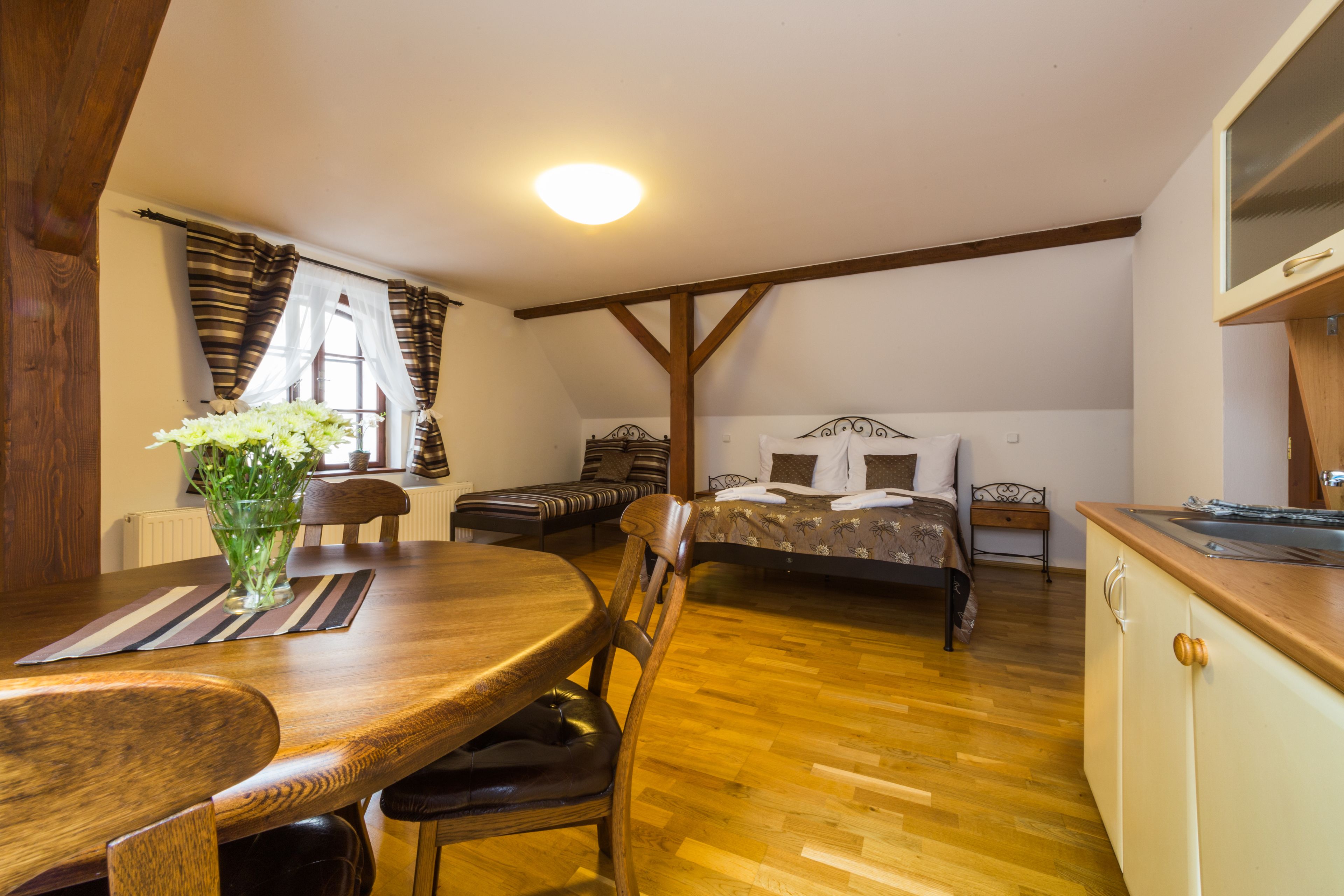 Um quarto aconchegante com uma mesa de jantar de madeira, uma cama com encosto e uma área de cozinha compacta.
