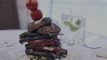 Uma pilha de legumes e um tomate cereja num prato, com um copo de água ao fundo.