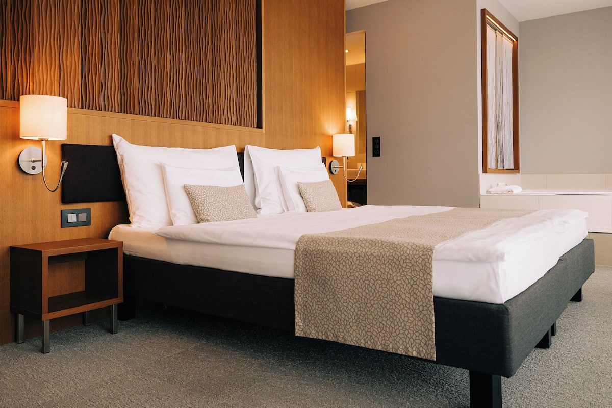 Quarto de hotel com uma cama grande, duas mesas de cabeceira, um painel de madeira na cabeceira e um espelho.