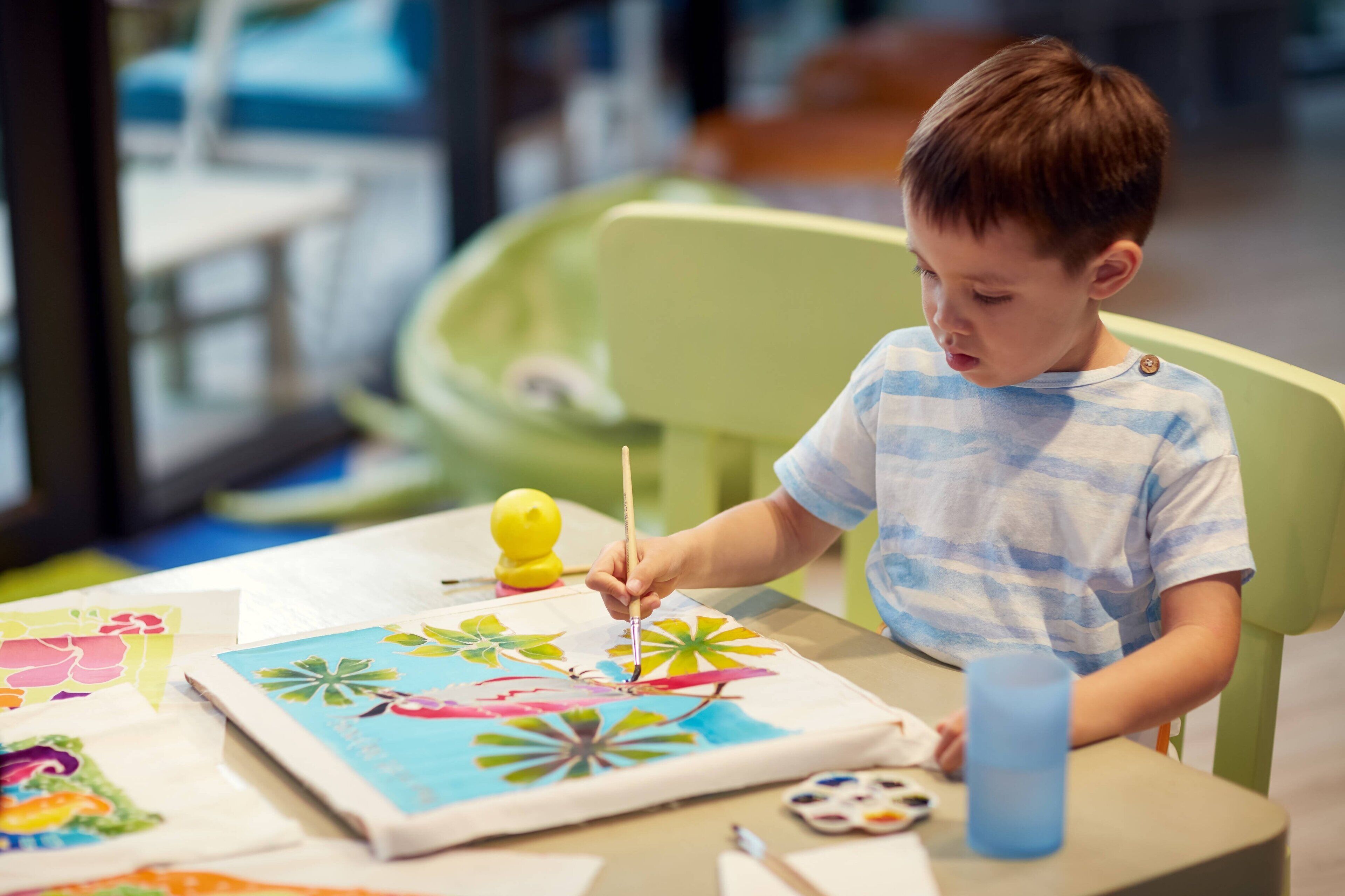 Criança pintando em uma mesa com materiais de arte.