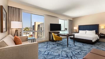 Quarto de hotel com cama, escrivaninha, televisão, sofá e vista da cidade.