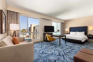 Quarto de hotel com cama, escrivaninha, televisão, sofá e vista da cidade.