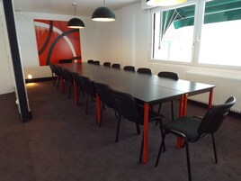 Uma sala de conferência com uma mesa comprida, cadeiras pretas e iluminação pendente.