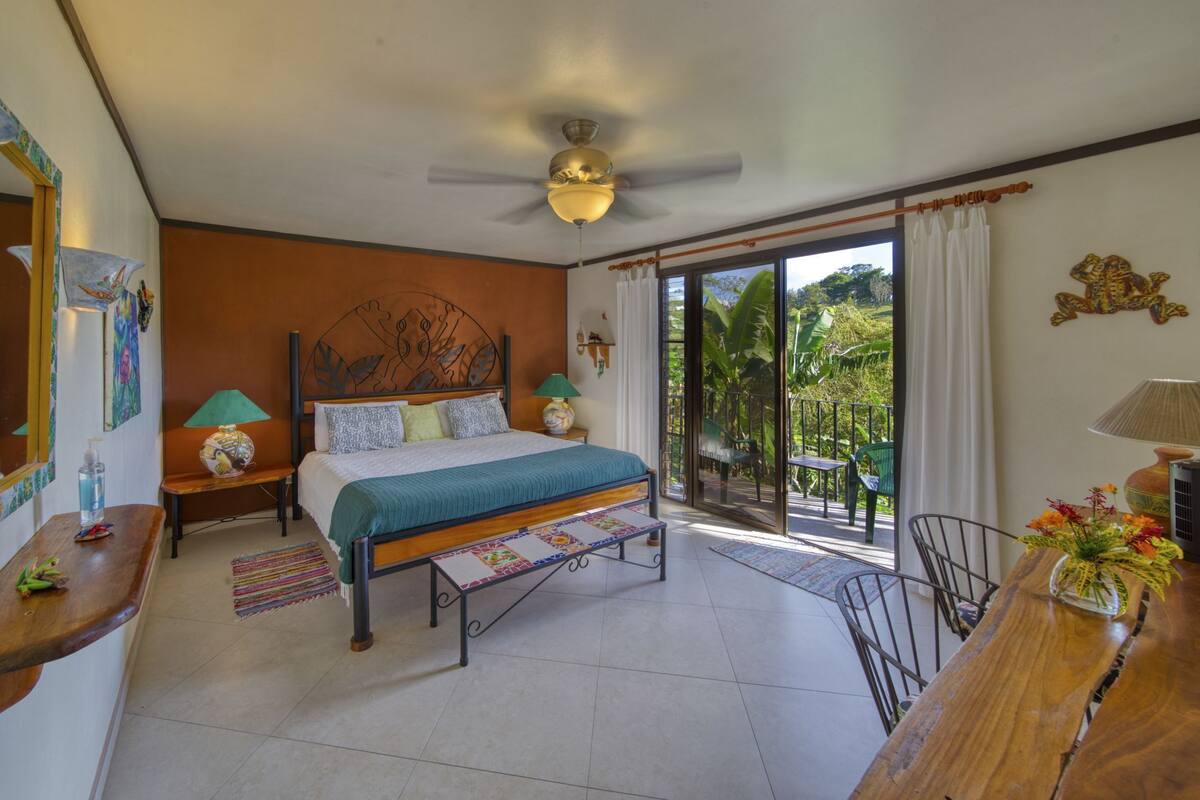 Quarto com cama, mesa de cabeceira, escrivaninha, cadeira, janela e ventilador de teto.