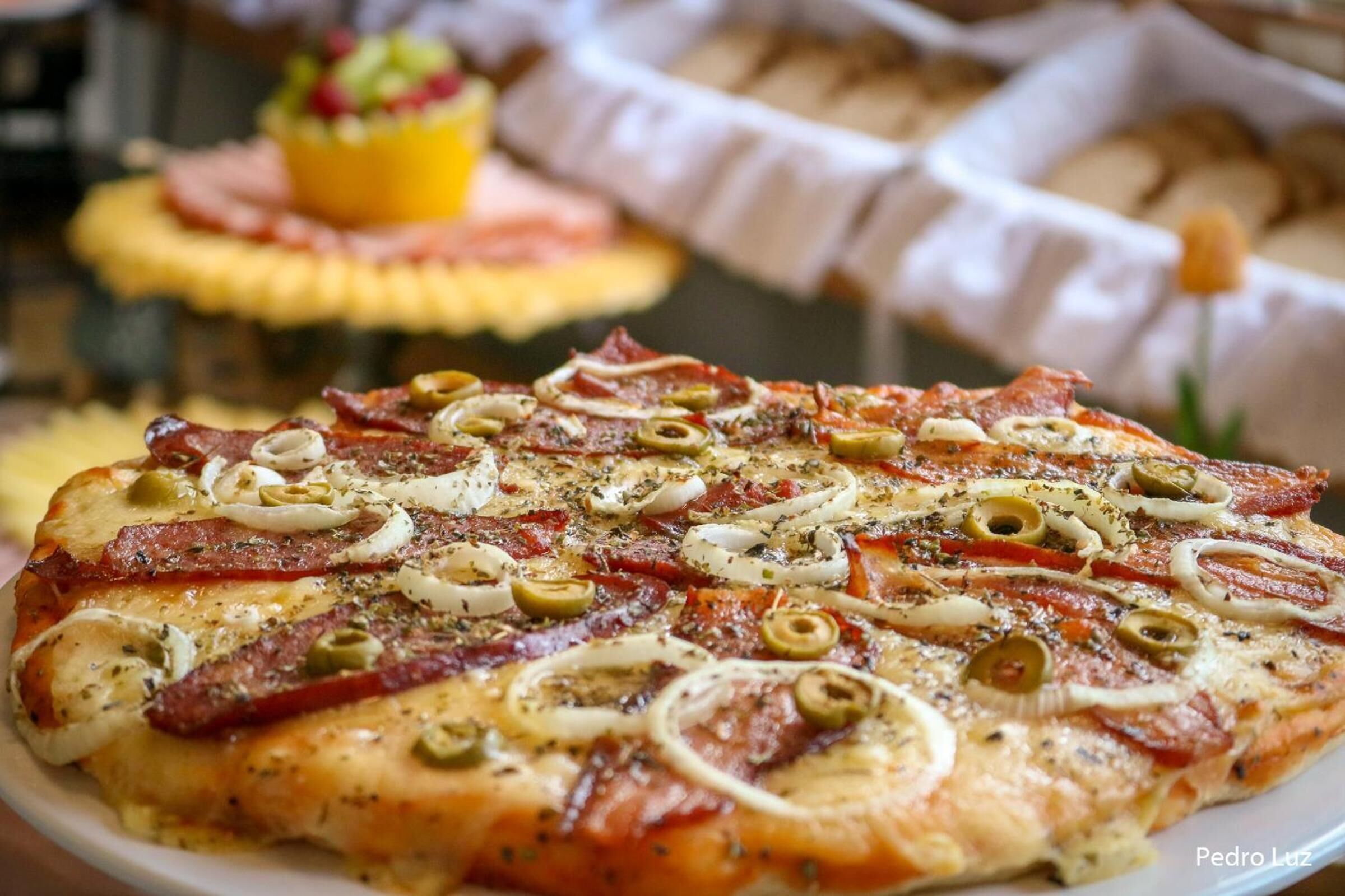 Pizza com azeitonas, cebolas e bacon em um prato branco.