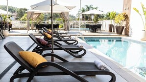 Área junto à piscina com espreguiçadeiras, guarda-sóis e piscina.