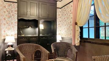 Um quarto com um armário de madeira escura, cadeiras de vime, uma mesa de vidro e uma janela com cortinas.