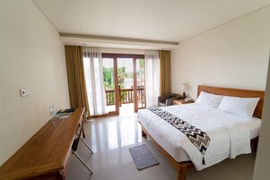 Quarto de hotel com cama, escrivaninha, cadeira, mesa de cabeceira e vista para o exterior.