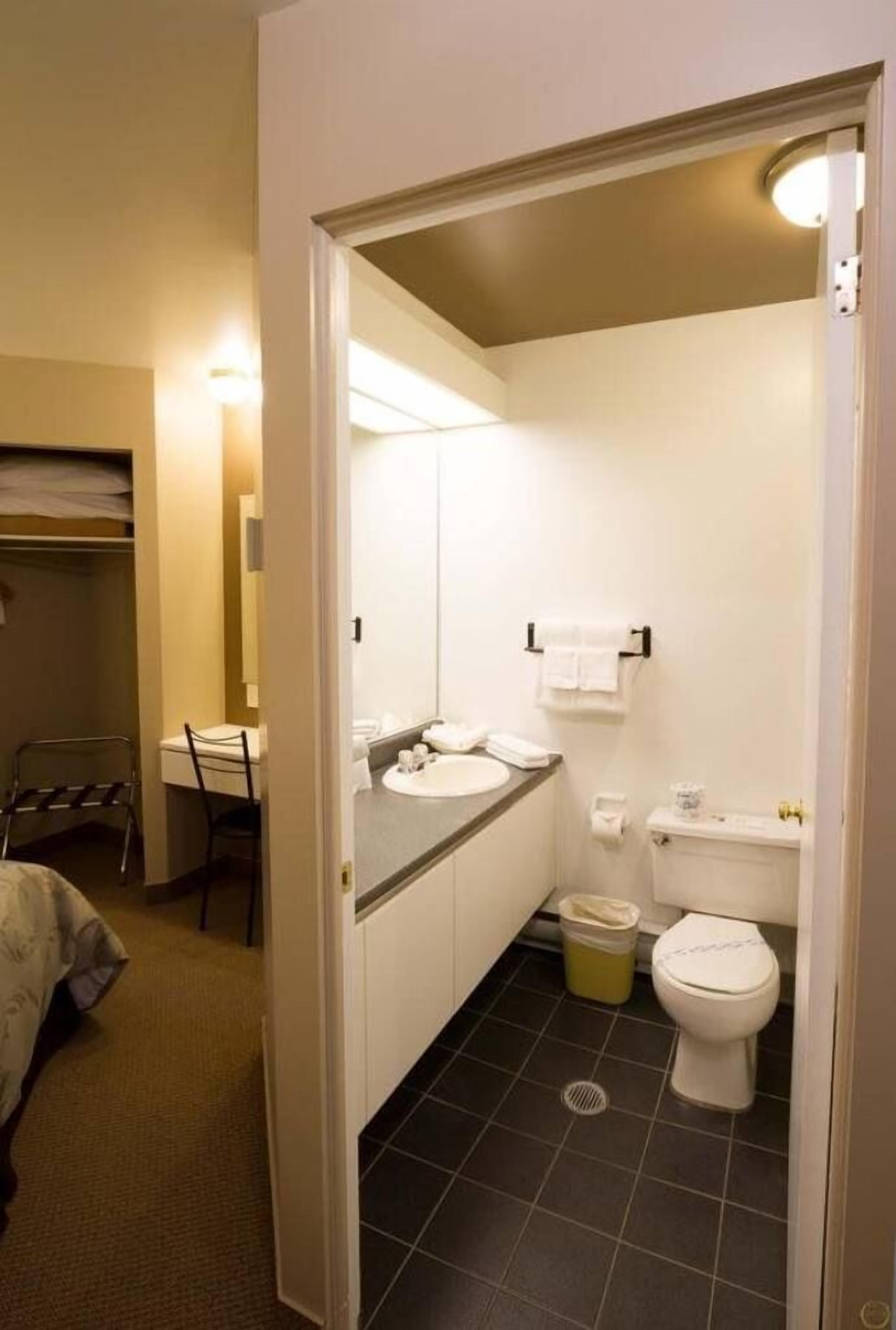 Casa de banho de hotel compacta com sanita, lavatório e um pequeno contentor de lixo.
