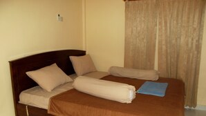 Cama bem arrumada com cabeceira marrom e roupa de cama bege em quarto com paredes lisas e cortina.