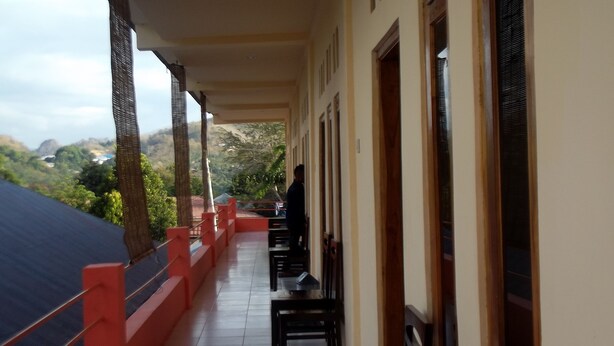 Uma varanda com piso de azulejos, guarda-corpos vermelhos e uma pessoa próxima à porta.