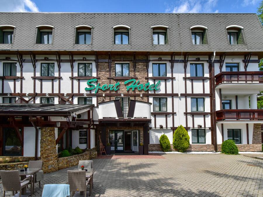Um hotel com estilo arquitetônico europeu tradicional, apresentando uma entrada imponente com uma placa, área externa para sentar e um jardim bem cuidado.