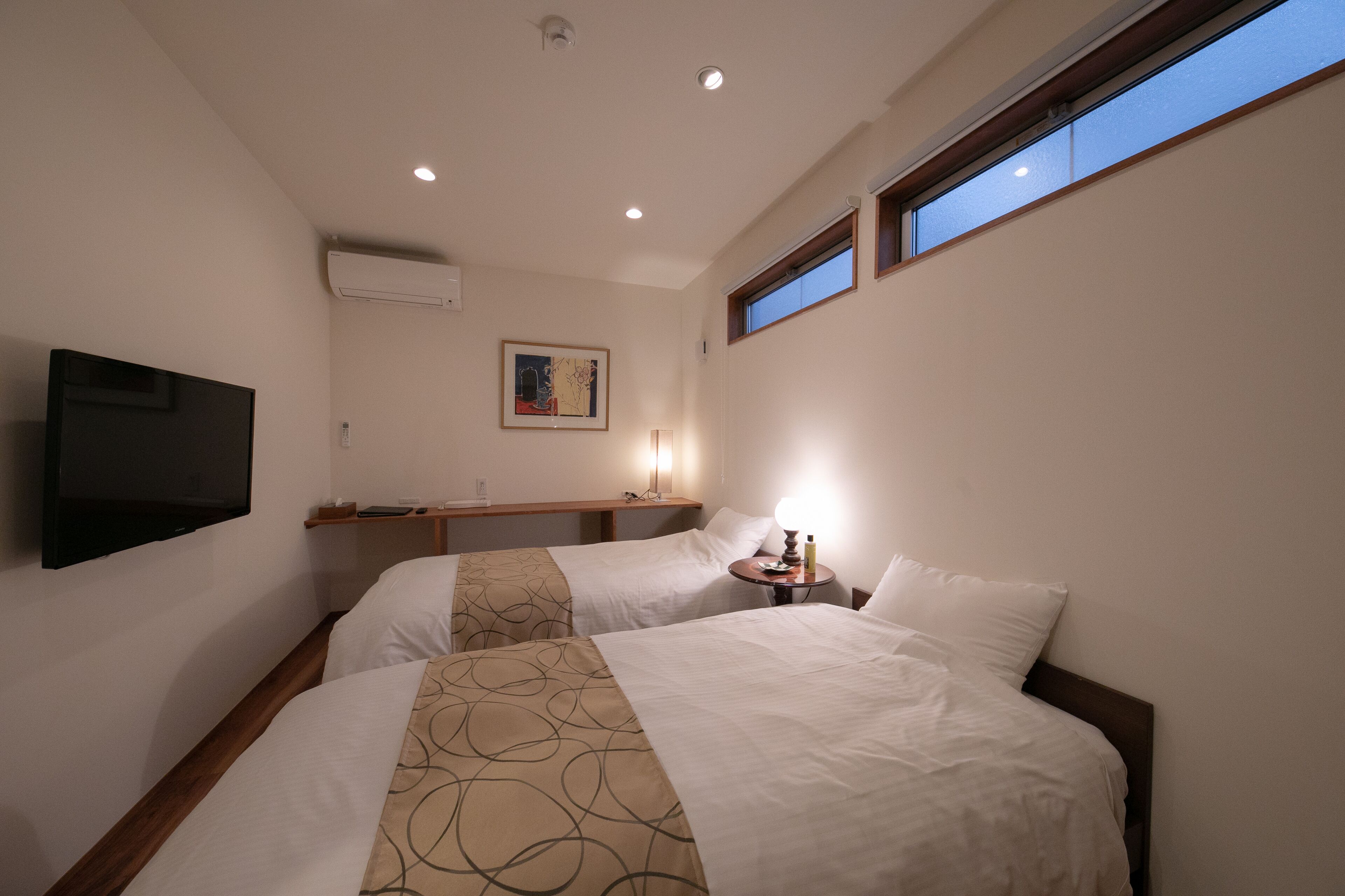 Quarto de hotel com duas camas, televisão, mesa de cabeceira com abajur e um quadro na parede.