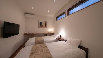 Quarto de hotel com duas camas, televisão, mesa de cabeceira com abajur e um quadro na parede.