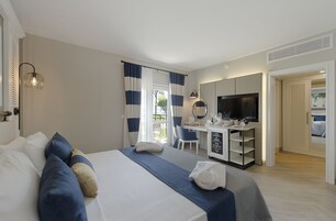 Quarto de hotel com cama, escrivaninha com computador, televisão e armário.