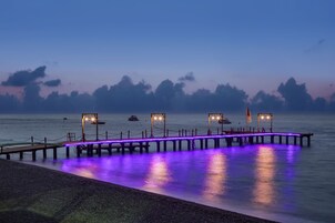 Um cais iluminado com luzes roxas que se estende sobre águas calmas, sob um céu límpido.
