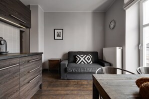 Cozinha moderna com armários de madeira escura, um sofá cinza com almofada estampada e uma mesa de jantar de madeira.