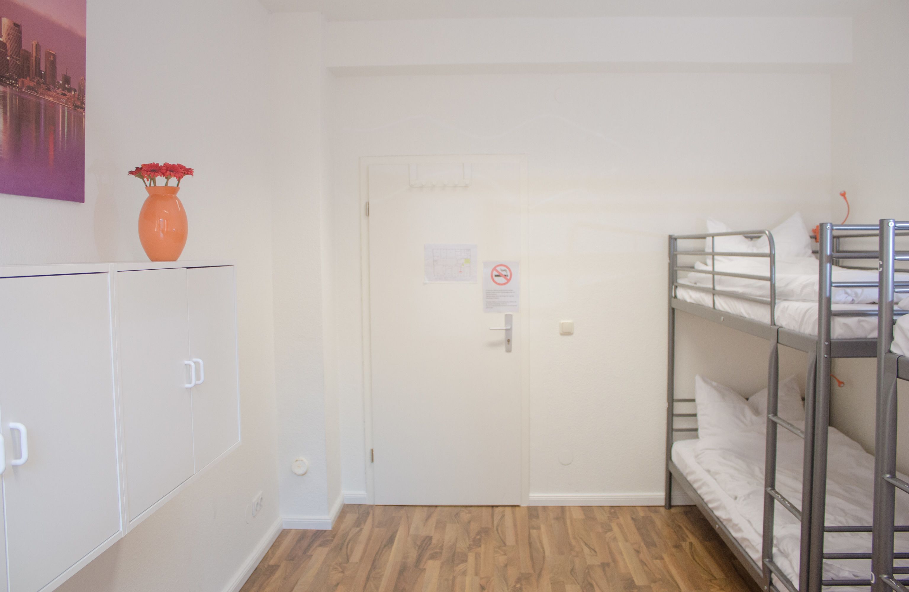 Quarto com beliches, um guarda-roupa branco e uma porta com uma placa.