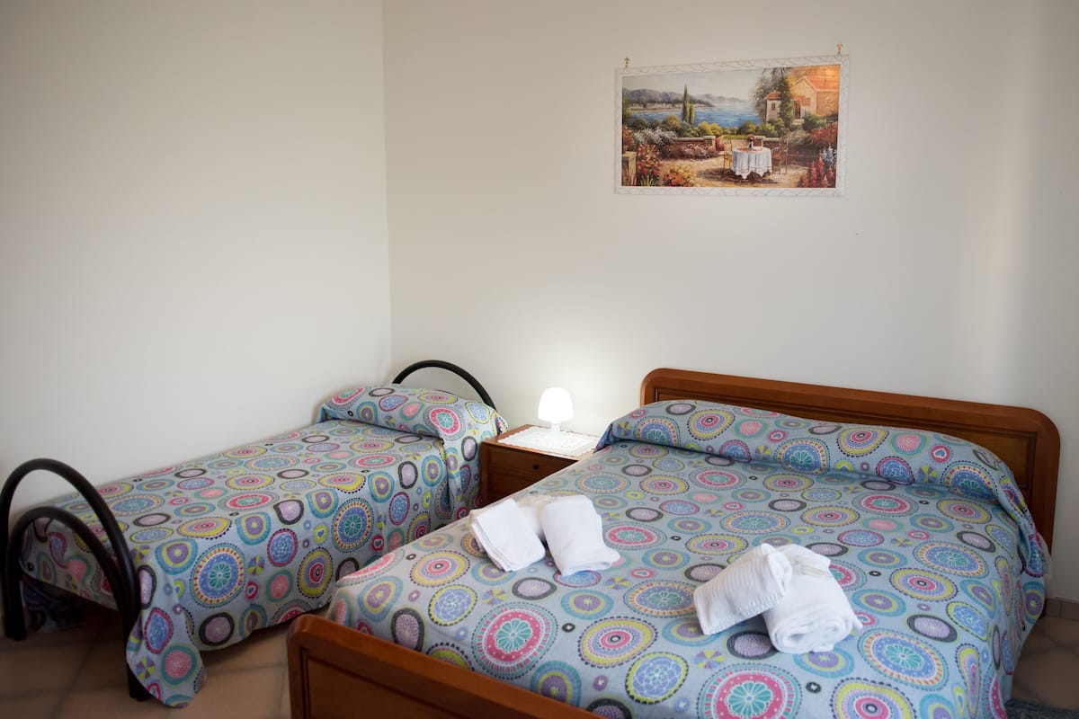 Quarto com duas camas de solteiro, cada uma com roupa de cama estampada e mesa de cabeceira com abajur.