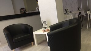 Quarto moderno com duas poltronas de couro preto, uma pequena mesa branca e um quadro branco com um cartaz.