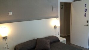 Quarto de hotel com uma cama, duas luminárias de cabeceira, um criado-mudo e uma porta com o número 103.