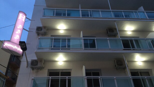 Um hotel com várias andares, varandas, aparelhos de ar condicionado e um letreiro de neon.
