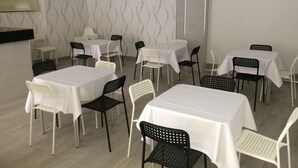Uma sala de jantar com várias mesas e cadeiras, parede com padrão e piso em tom claro.