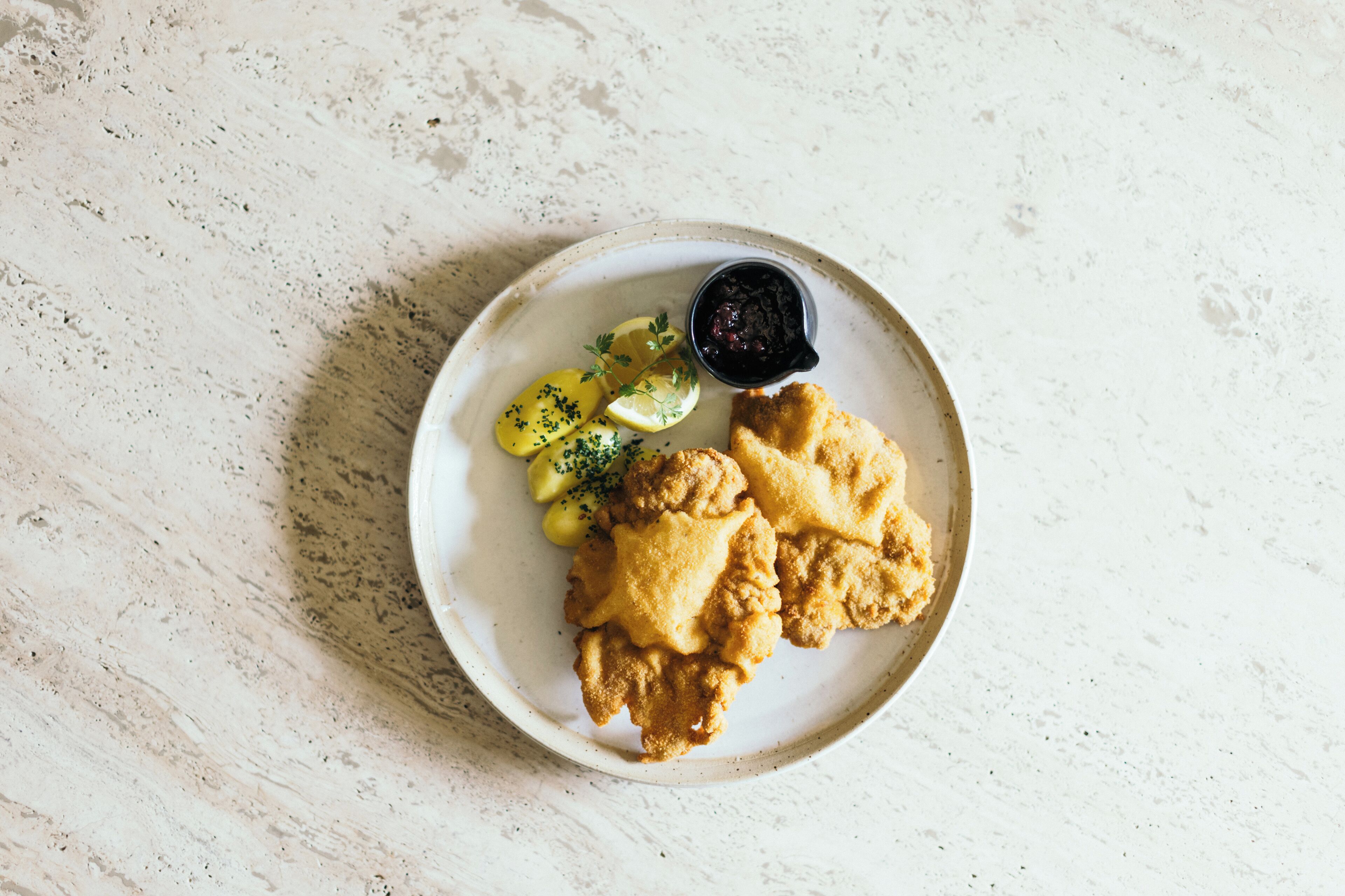 Um prato com frango frito, fatias de limão e picles.