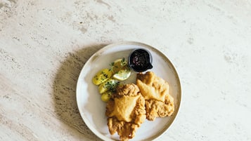 Um prato com frango frito, fatias de limão e picles.