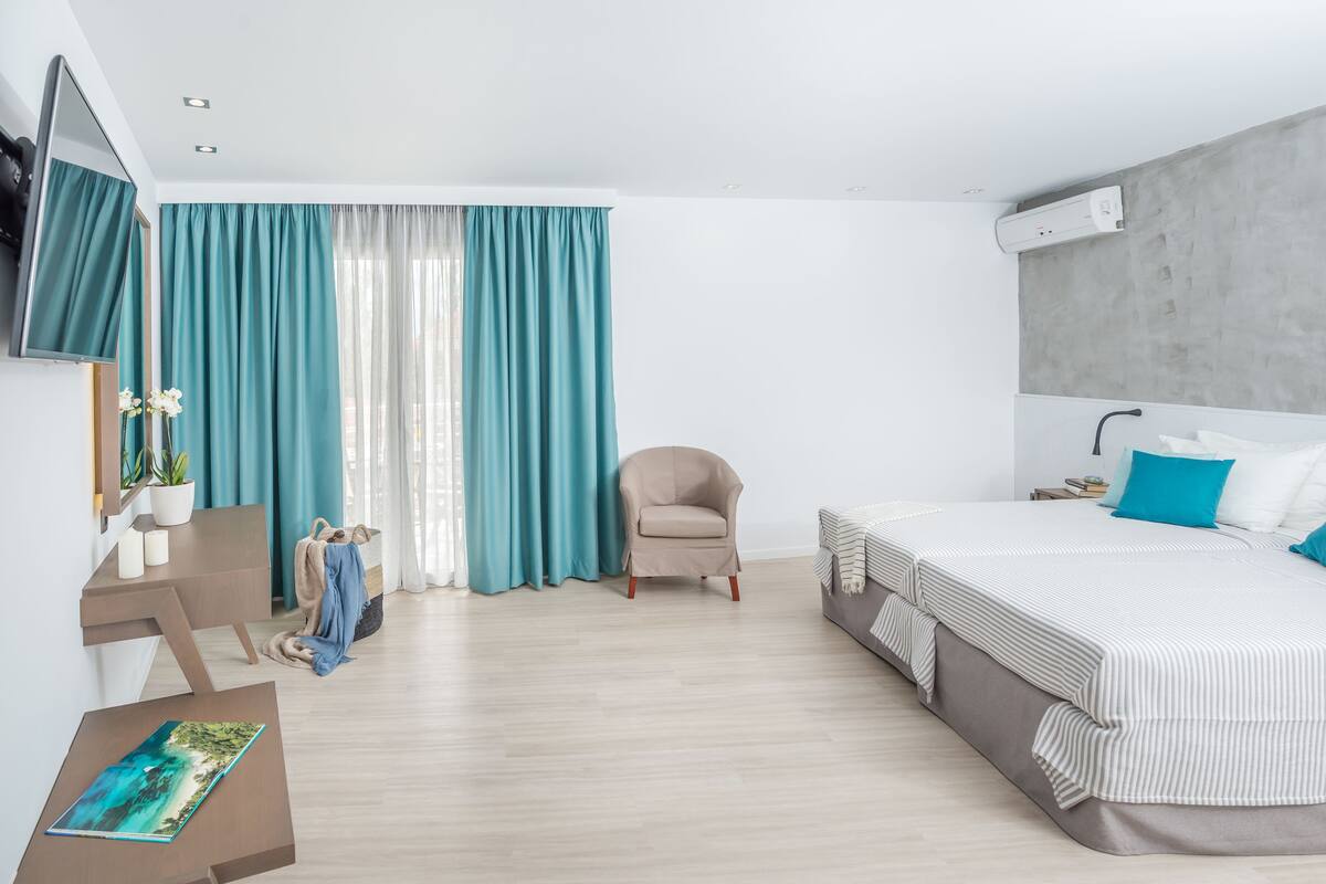Quarto de hotel moderno com uma cama grande, uma poltrona, uma escrivaninha e uma televisão.