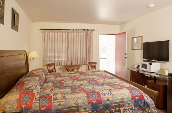 Quarto de hotel com uma cama grande, uma secretária com televisão, uma cadeira e uma janela com cortinas.