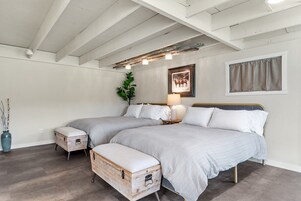 Quarto com duas camas, um baú de madeira, uma planta e um quadro pendurado na parede.