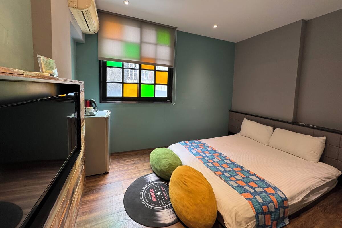 Quarto moderno com cama, escrivaninha, cadeira e janela com painéis coloridos.
