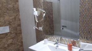 Casa de banho com parede de pedra, lavatório branco, espelho e cabine de duche com porta de vidro.