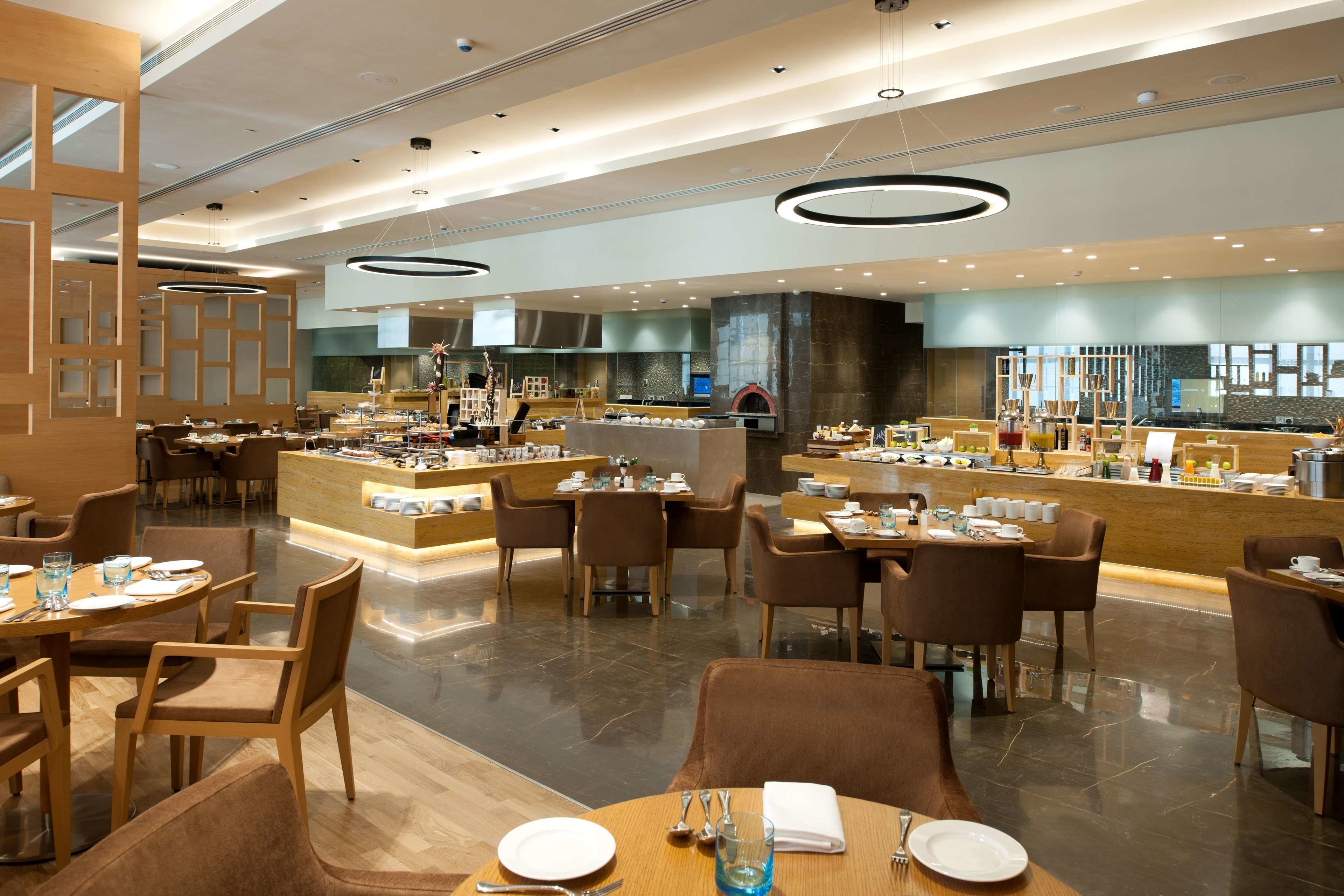 Um restaurante moderno com mesas redondas, cadeiras marrons e um balcão central.