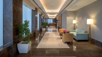 Um hall de hotel moderno com piso de mármore, balcão de recepção, sofá, poltrona e planta em vaso.