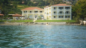 Um edifício de dois andares com telhado de telhas vermelhas, varanda e área de piscina com espreguiçadeiras.