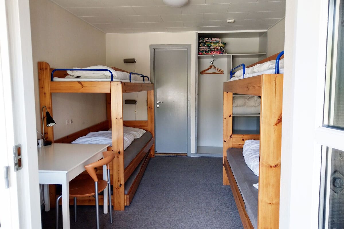 Quarto de dormitório com beliches, escrivaninha, cadeira e guarda-roupa.